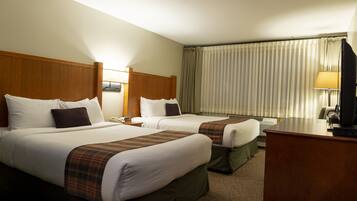 Quarto de hotel com duas camas, uma escrivaninha, uma lâmpada e uma televisão.