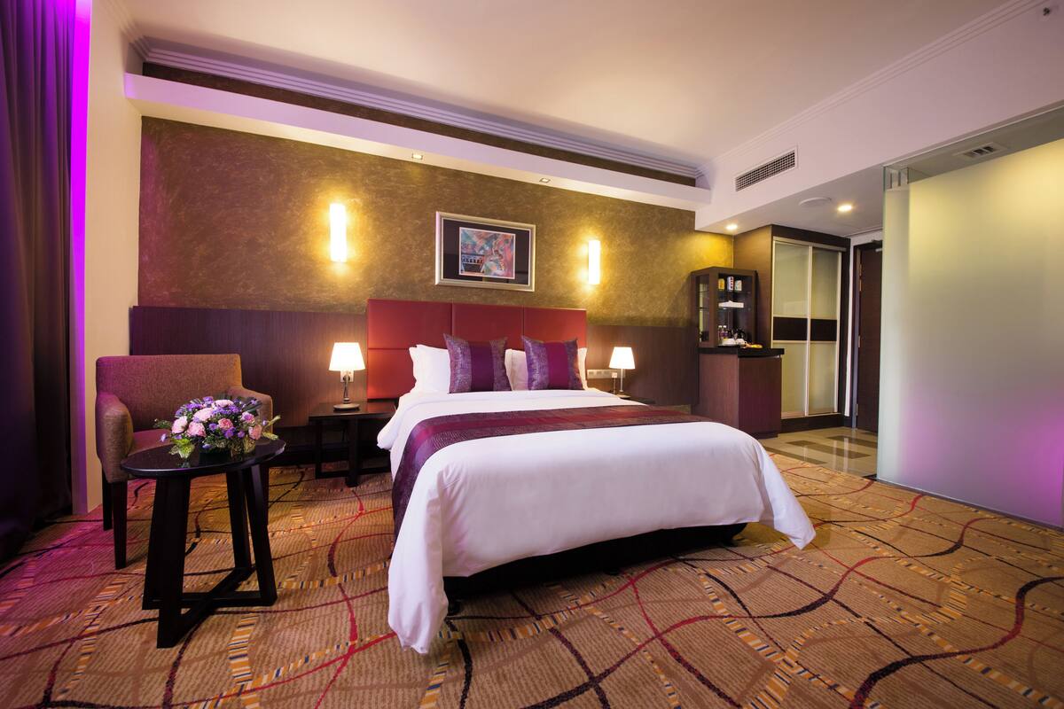 Quarto de hotel com uma cama grande, uma cadeira, uma mesa de cabeceira e uma escrivaninha.