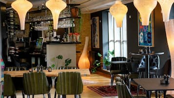 Interior de restaurante com área de bar, mesas de madeira, cadeiras verdes e luminárias pendentes.