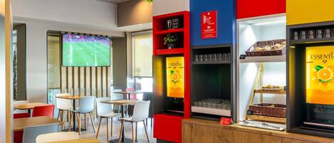 Um café moderno com tela para esportes, área de estar e balcão com diversos produtos.