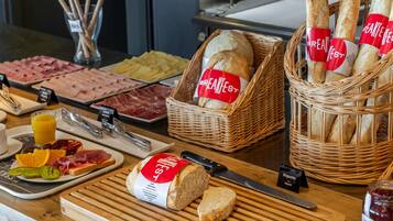 Buffet de café da manhã com diversos tipos de carne, pães e frutas.