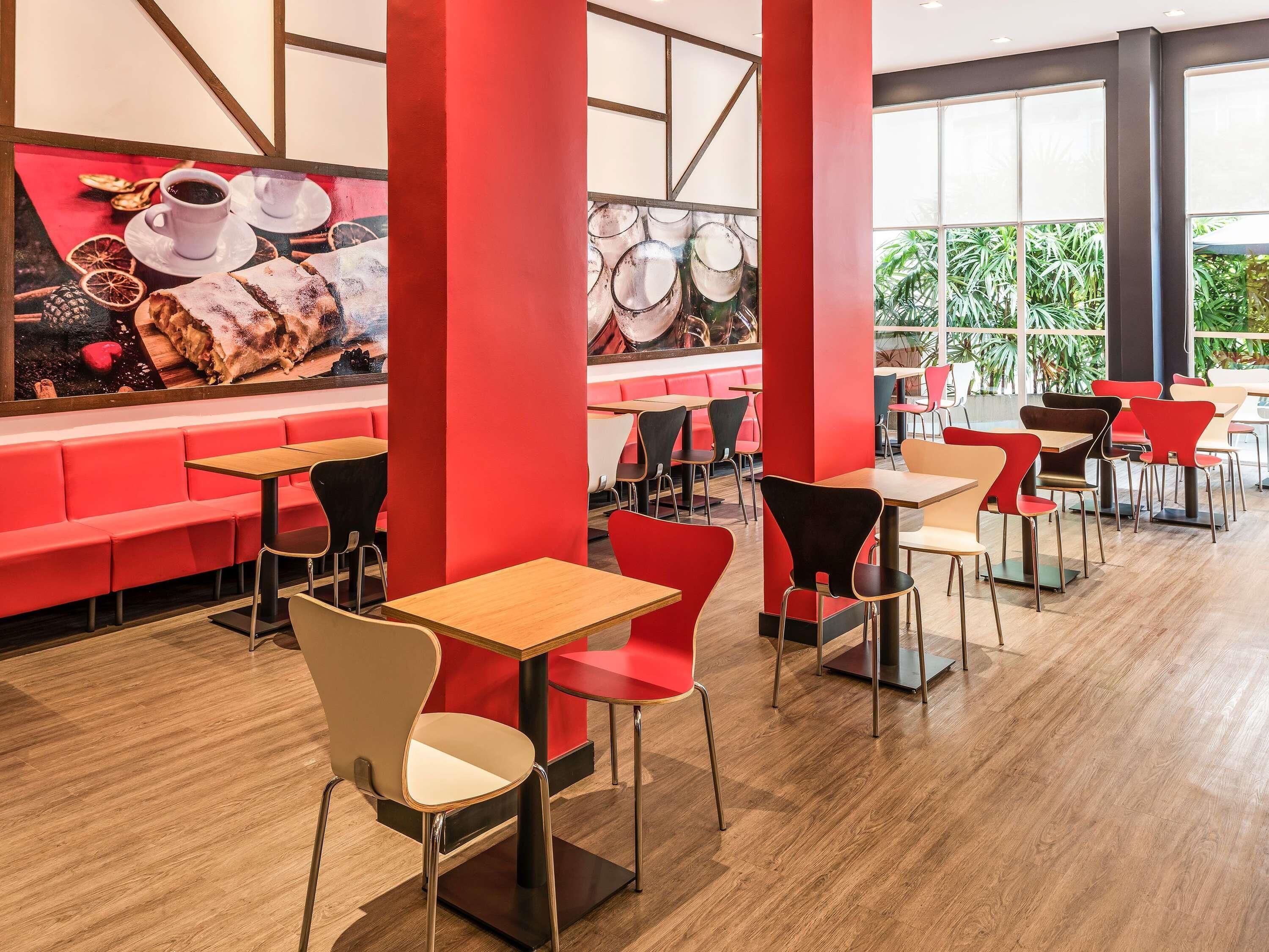 Interior moderno de restaurante com assentos vermelhos, mesas de madeira e grandes janelas.