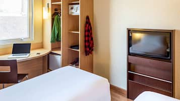 Quarto de hotel compacto com uma cama, uma escrivaninha com um laptop, uma TV, micro-ondas e um guarda-roupa.