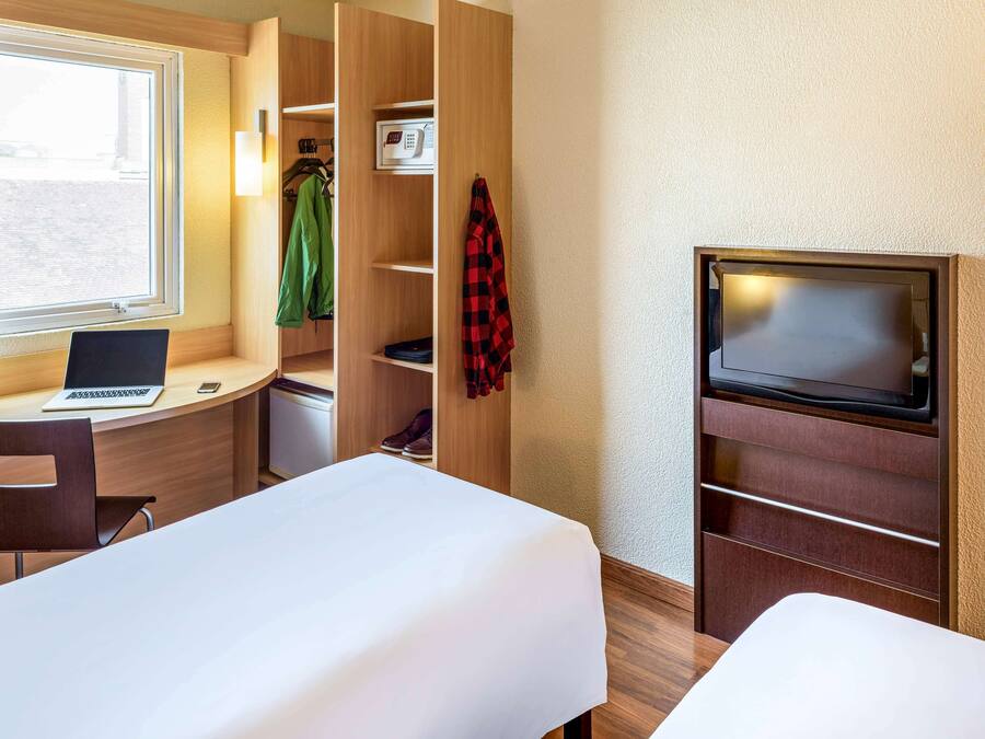 Quarto de hotel compacto com uma cama, uma escrivaninha com um laptop, uma TV, micro-ondas e um guarda-roupa.