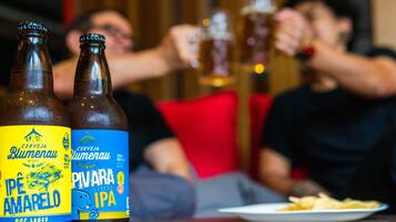 Duas garrafas de cerveja sobre uma mesa, com um prato de comida e uma pessoa ao fundo.