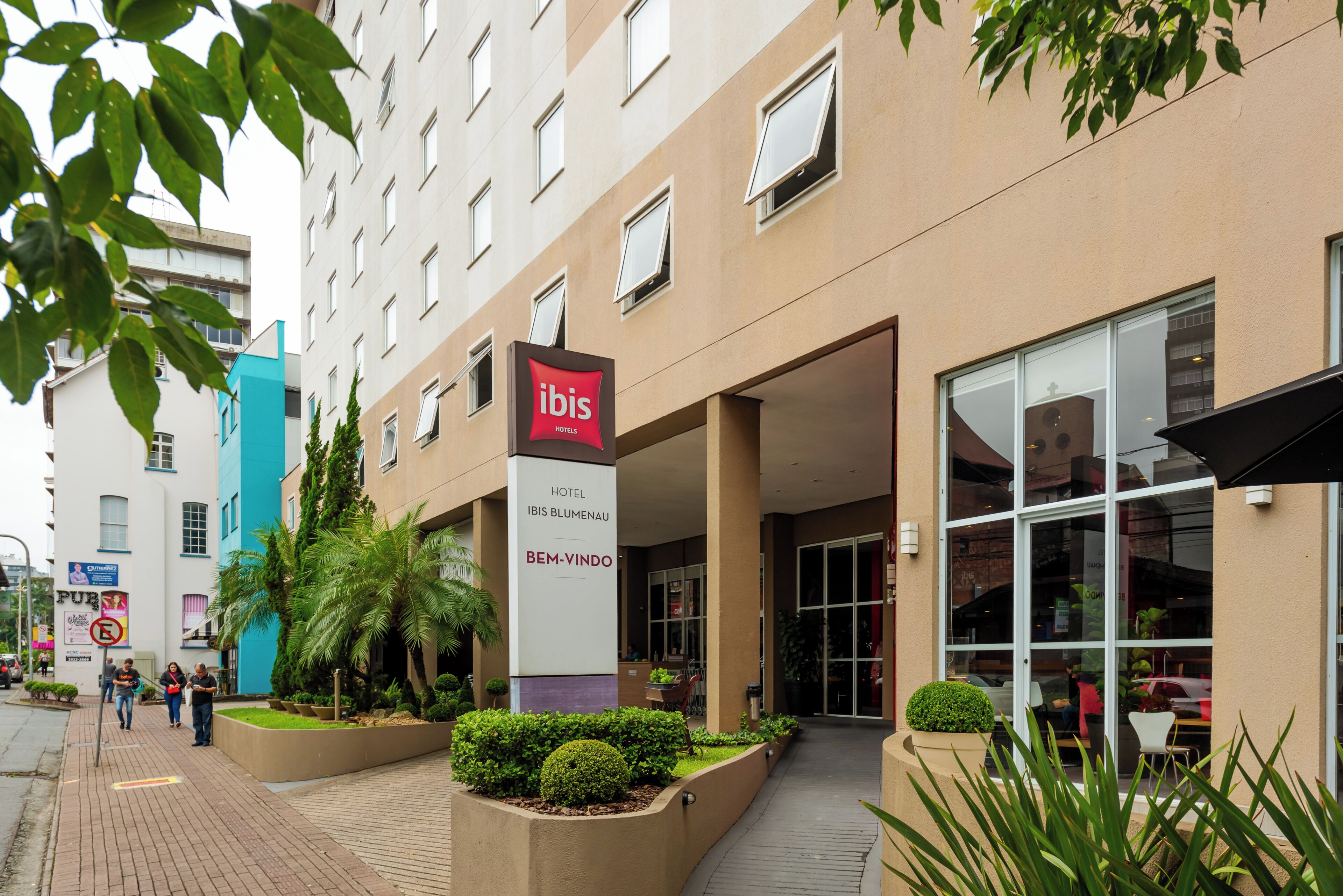 Entrada de hotel com placa da ibis hotels, um caminho para pedestres e vegetação.