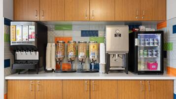 Uma área de cozinha com bebedouro, cafeteira, dispensadores de cereais, frigorífico e mini-frigorífico.