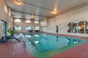 Piscina interna com água cristalina, rodeada por espreguiçadeiras e chão de tijolos.