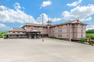 Um hotel grande e com vários andares, com entrada central, área de espera coberta e estacionamento.