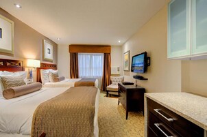 Quarto de hotel com duas camas, uma escrivaninha, televisão e uma janela grande com cortinas.