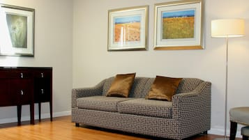 Uma sala de estar com um sofá estampado, um armário de madeira escura e três quadros na parede.