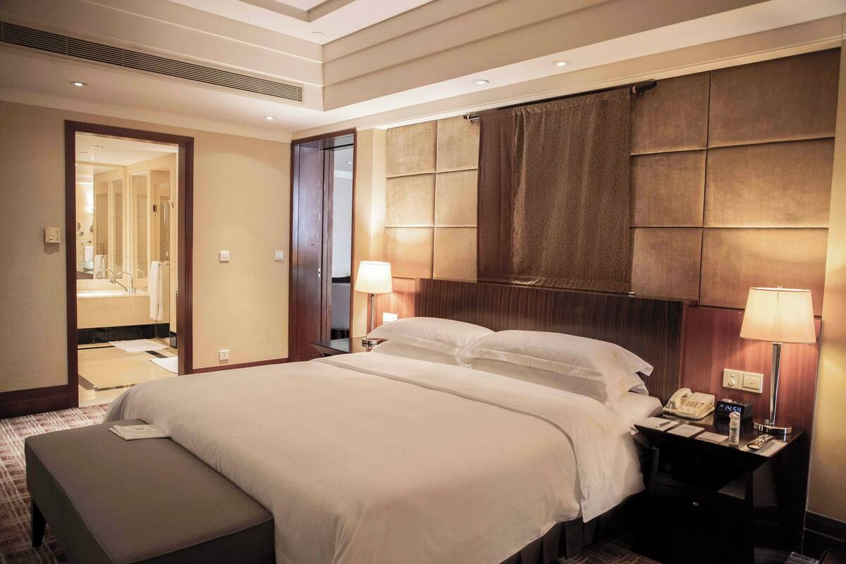 Quarto de hotel com uma cama grande, mesas de cabeceira, uma escrivaninha e um espelho.