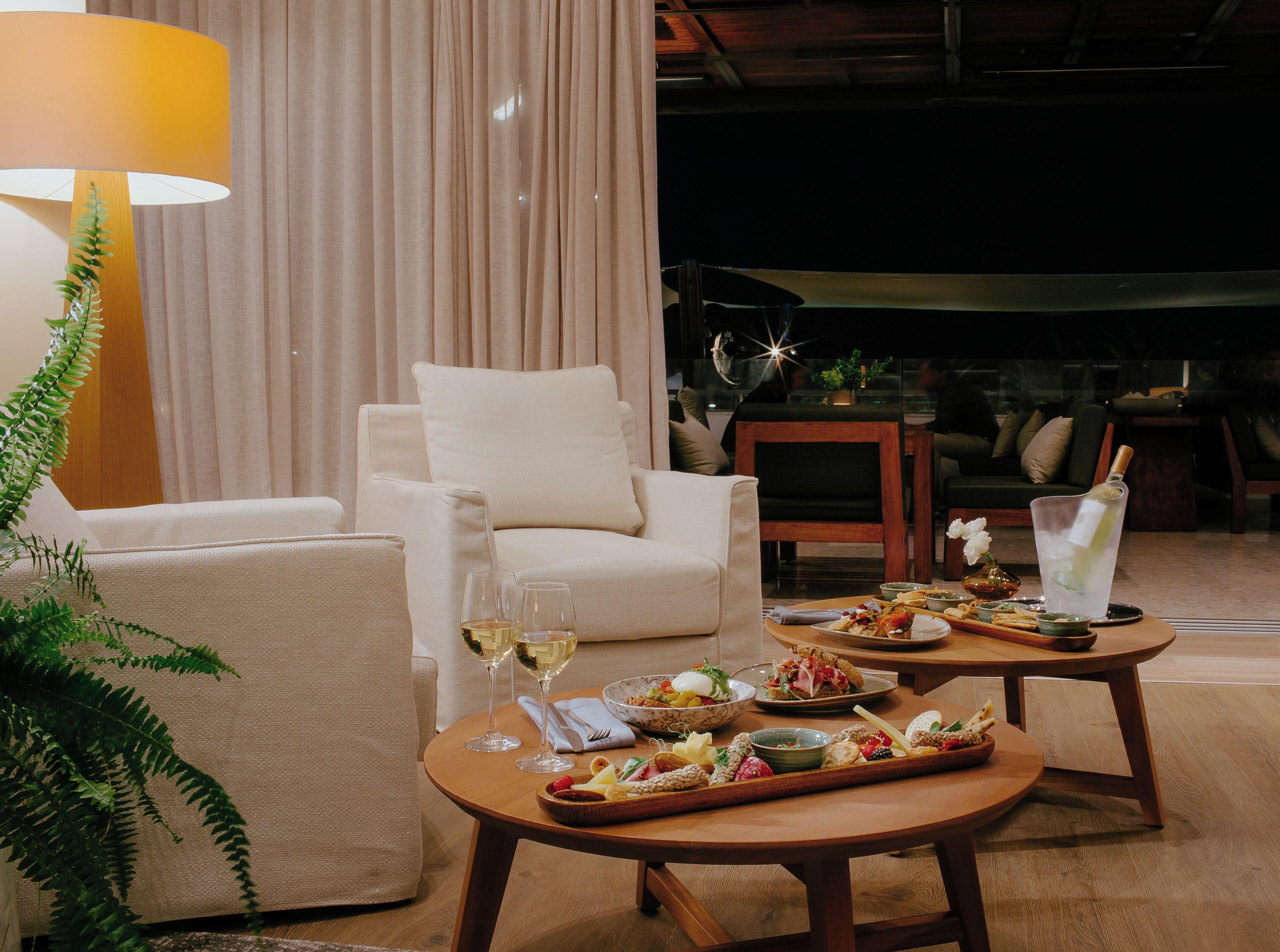 Uma sala de jantar com um sofá, uma mesa com comida e bebidas, e uma luminária.