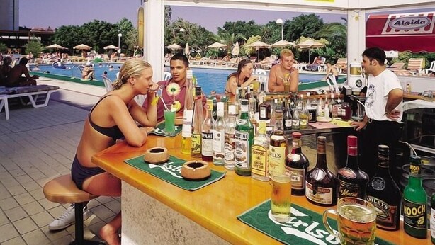 Uma área de bar com vista para a piscina, exibindo diversos tipos de bebidas e uma placa com o nome Carlotti's.