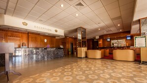 Uma área de recepção de hotel, com balcão de recepção, espaço para sentar e bar.