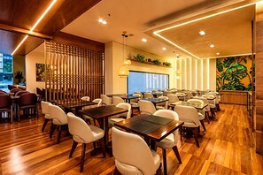 Um restaurante com piso de madeira, cadeiras brancas e mesas dispostas em um espaço amplo.