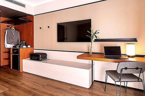 Quarto de hotel com guarda-roupa de madeira, secretária com um laptop, uma cadeira, um banco e uma TV fixada na parede.