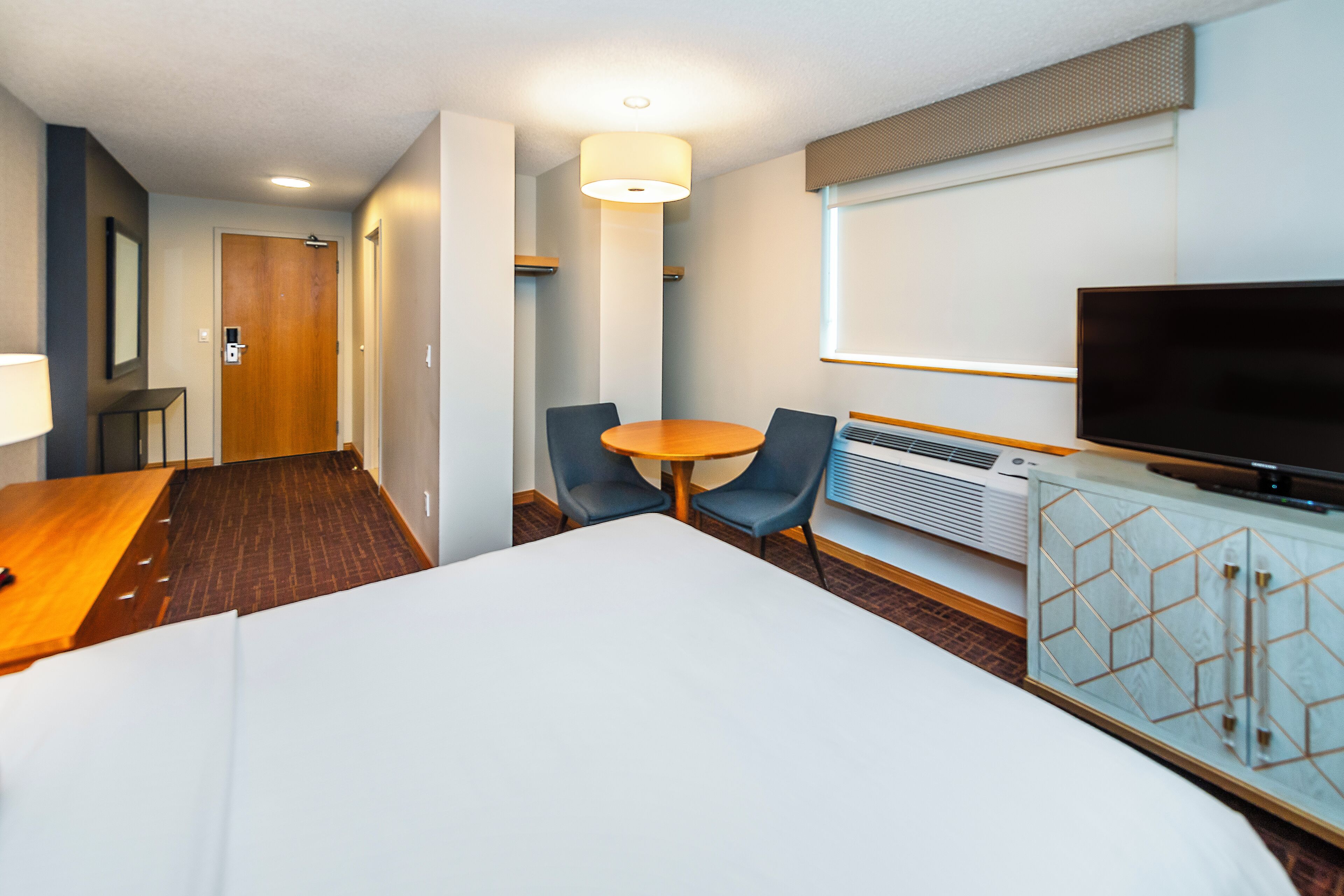 Quarto de hotel com cama, escrivaninha, cadeira, televisão e armário.