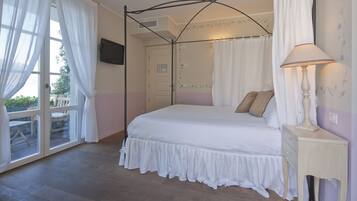 Quarto com cama de dossel, mesa de cabeceira com abajur e vista através de uma janela grande com cortinas.