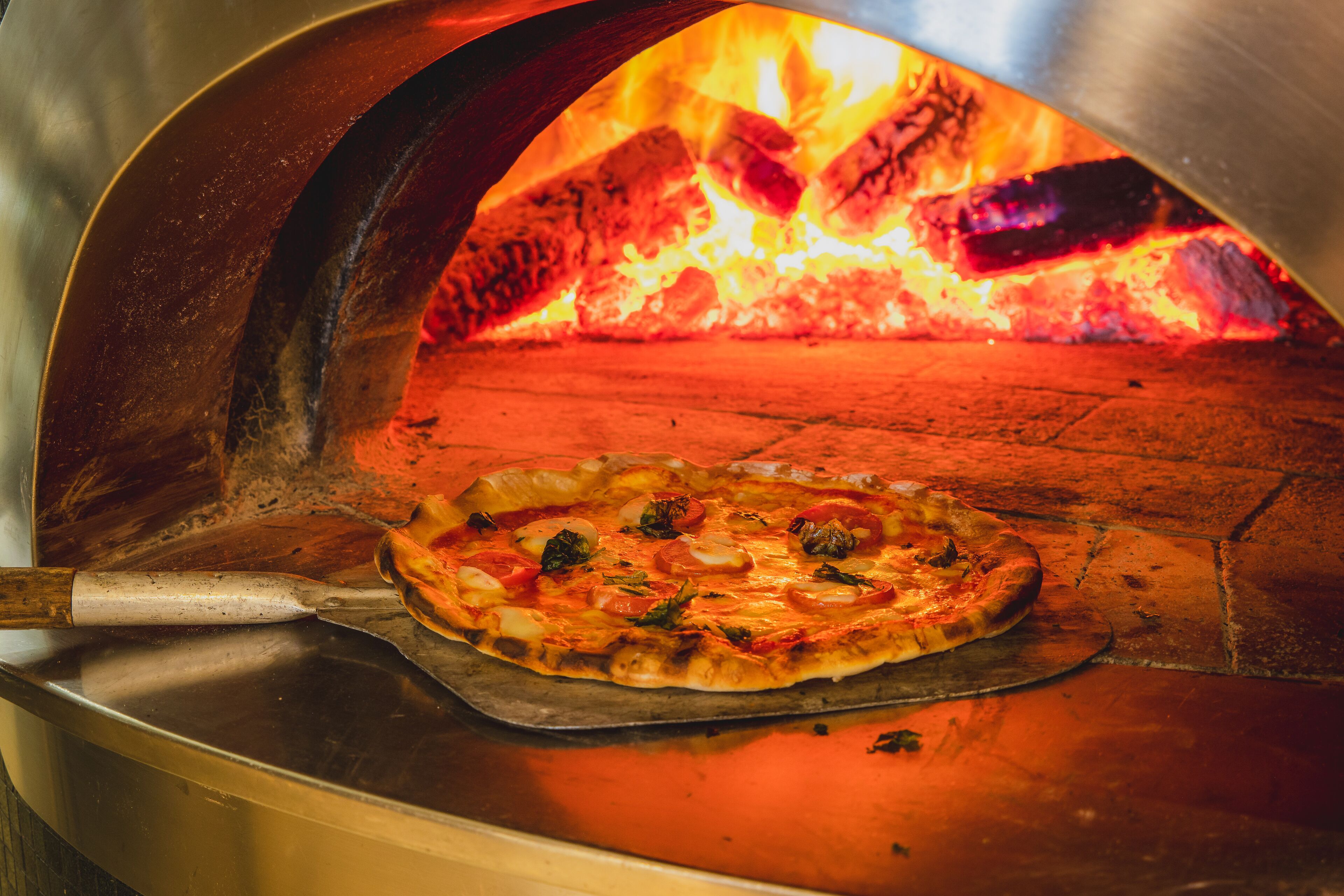 Uma pizza dentro de um forno a lenha, com chamas visíveis.