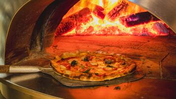 Uma pizza dentro de um forno a lenha, com chamas visíveis.