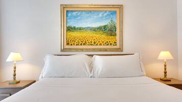 Quarto de hotel com uma cama, duas luminárias de cabeceira e um quadro de um campo.