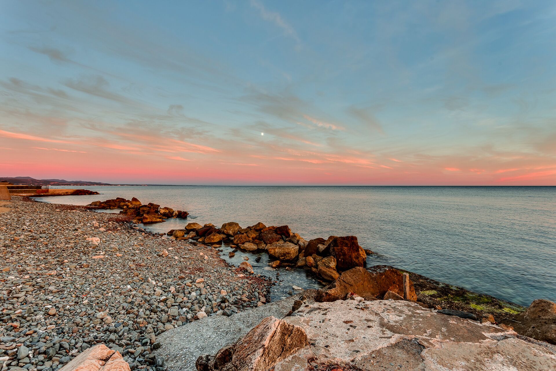 Uma costa rochosa com mar calmo e céu ao pôr do sol.