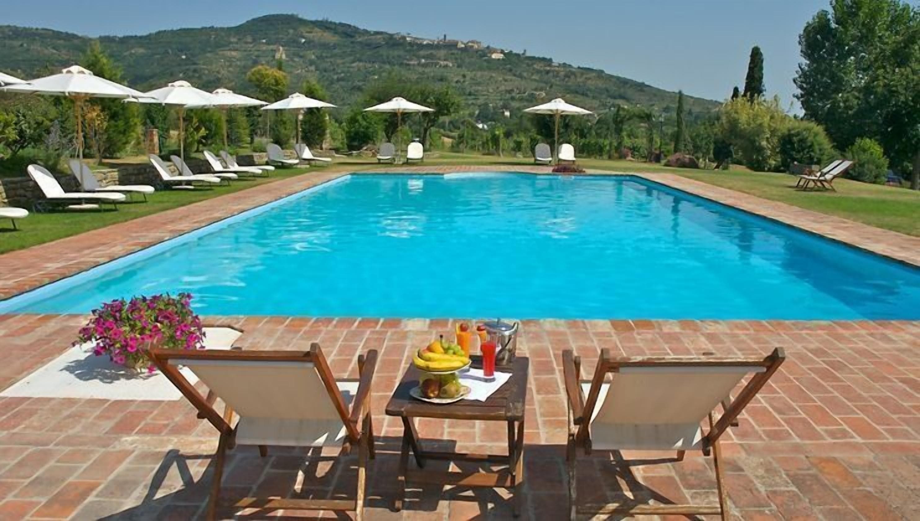 Piscina com espreguiçadeiras e guarda-sóis, rodeada por vegetação e colinas.