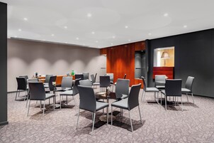 Uma sala de conferências com uma mesa redonda, cadeiras cinzentas e um tapete estampado.