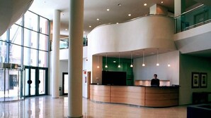 Um hall espaçoso com uma recepção em balcão curvo, pilares imponentes e teto alto.