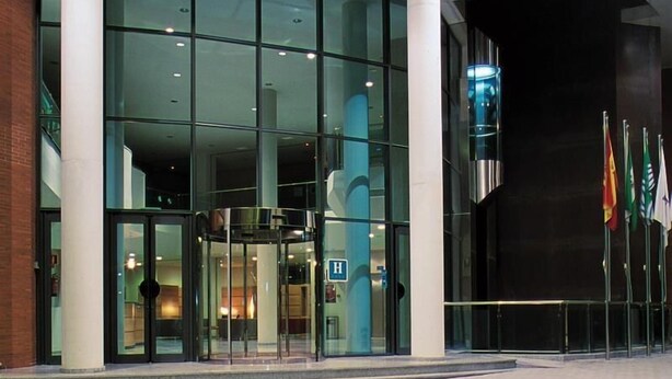 Um edifício moderno com grandes janelas de vidro e entrada por porta giratória.