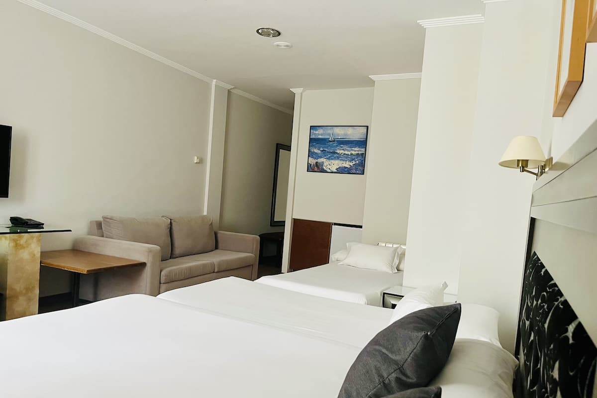 Quarto de hotel com cama, escrivaninha, cadeira e televisão.
