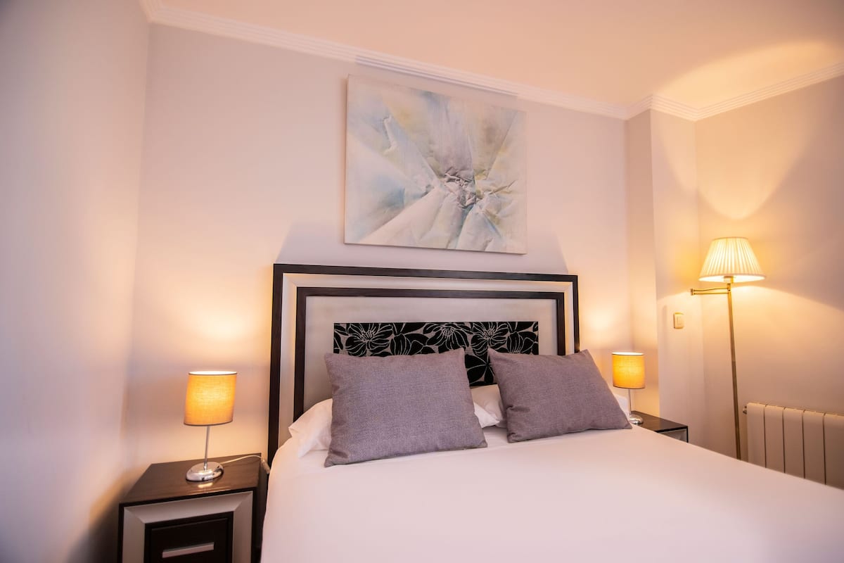 Cama bem arrumada com cabeceira, duas luminárias de cabeceira e uma obra de arte pendurada na parede.