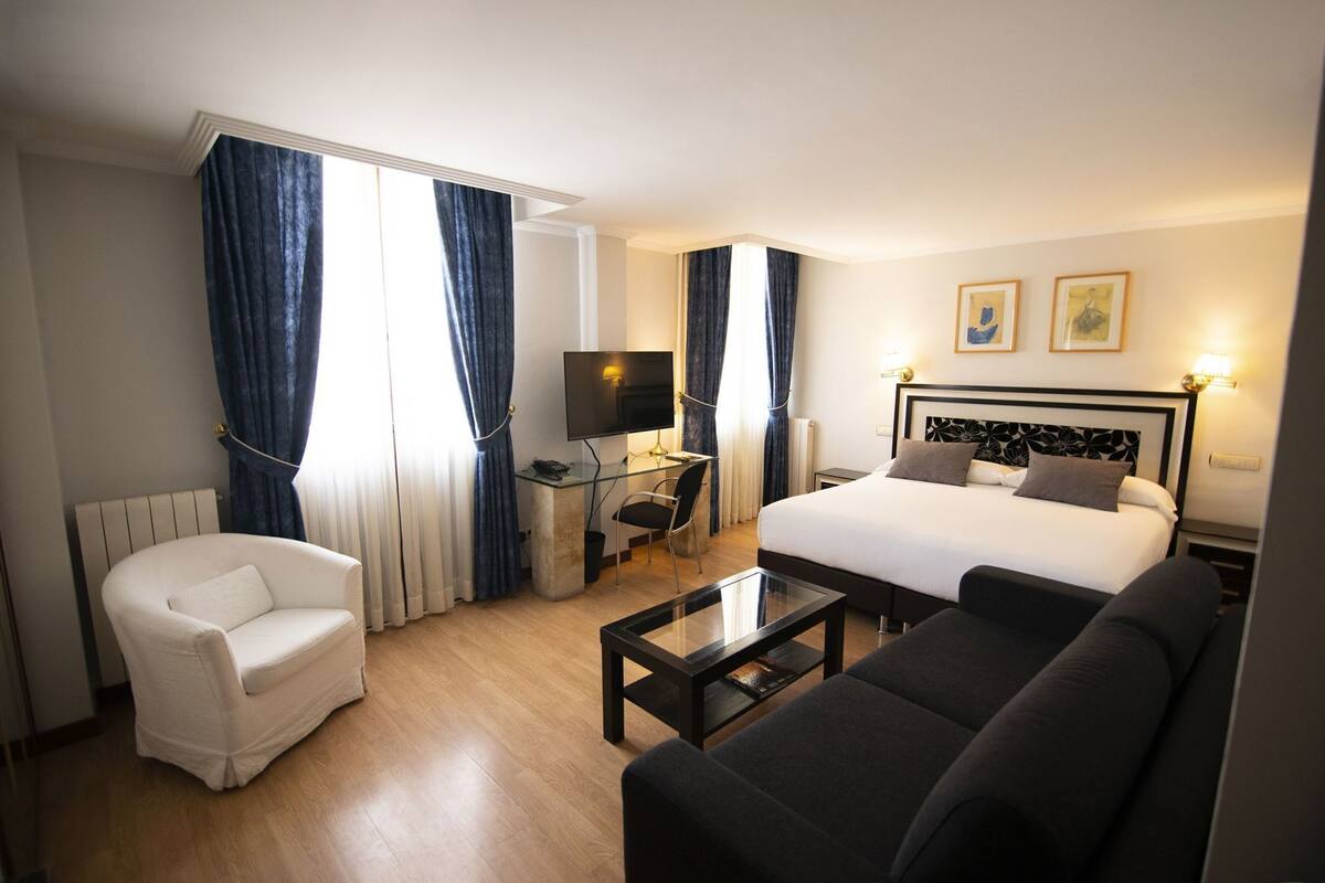 Quarto de hotel com cama, secretária com computador, cadeira, sofá e televisão.