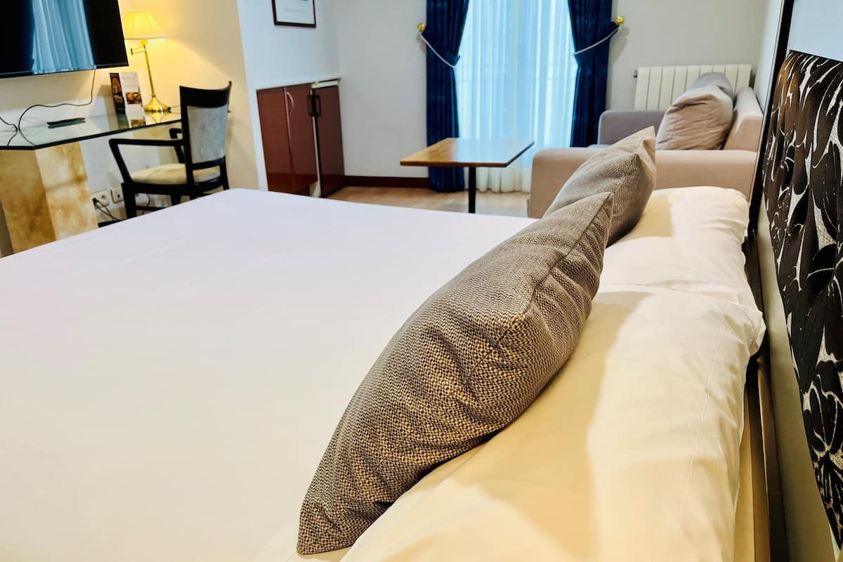 Quarto de hotel com uma cama grande, uma mesa com cadeira, uma mesinha e uma televisão.
