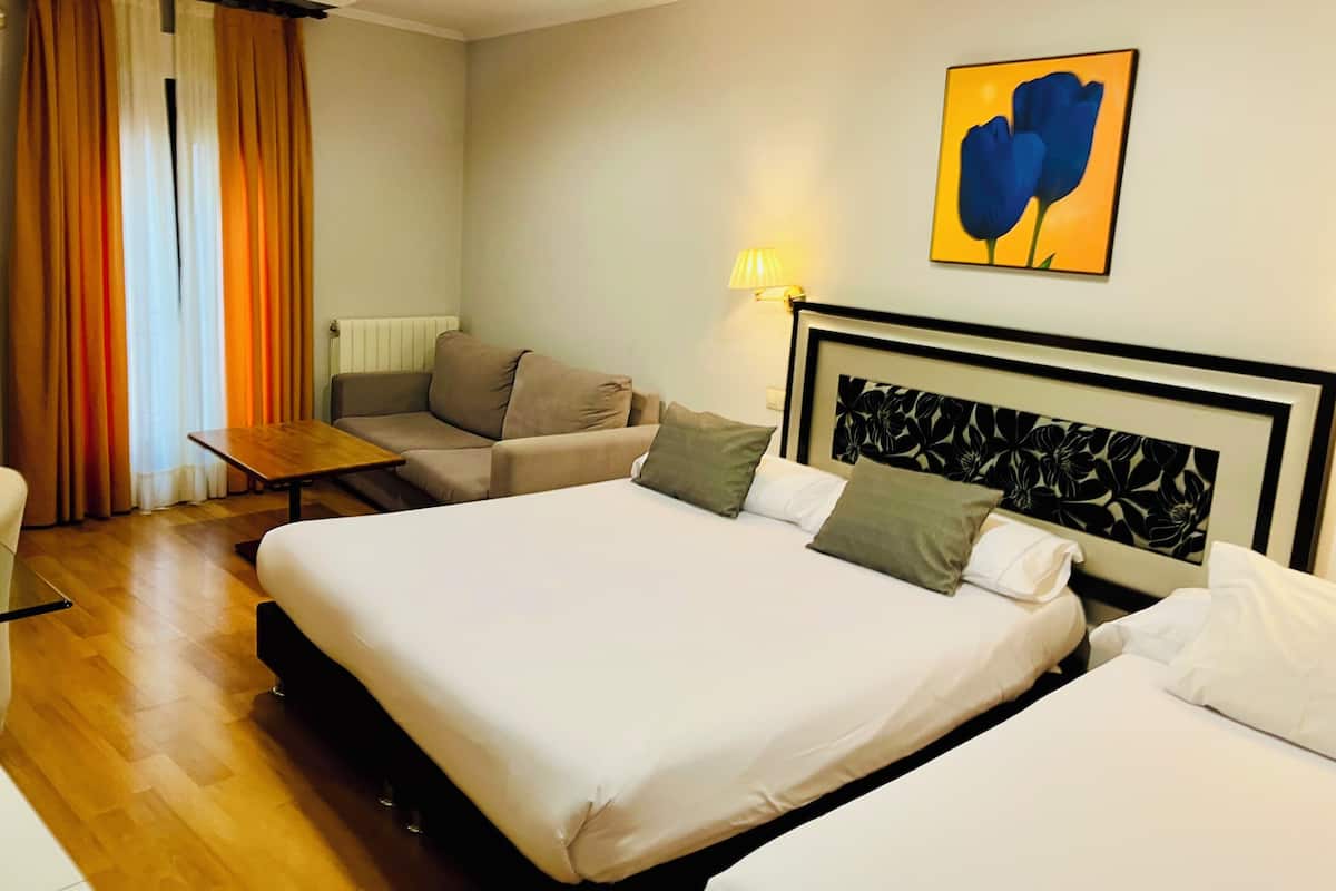 Quarto de hotel com uma cama grande, um sofá menor, uma mesa de centro de madeira e uma luminária.