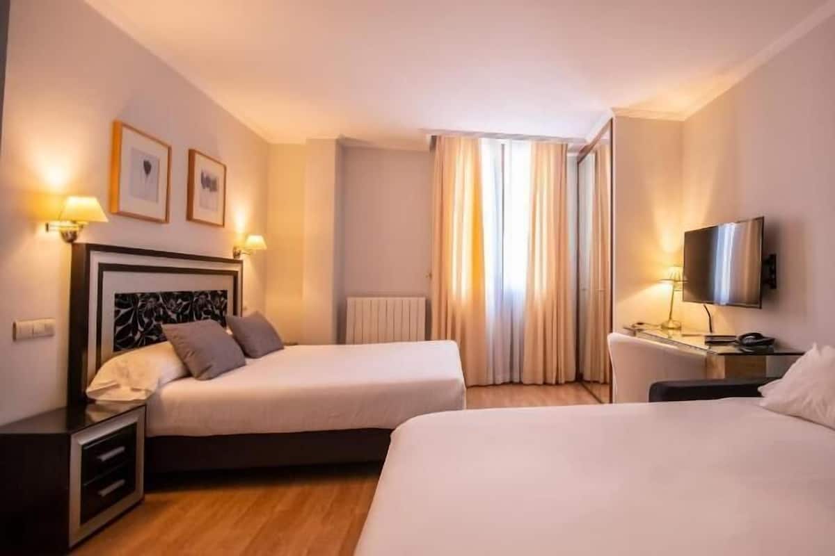 Quarto de hotel com duas camas, televisão, abajures e quadros nas paredes.