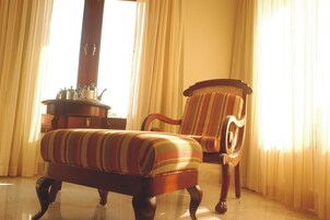 Quarto com uma cadeira de madeira, um banquinho listrado e uma mesa com um bule.