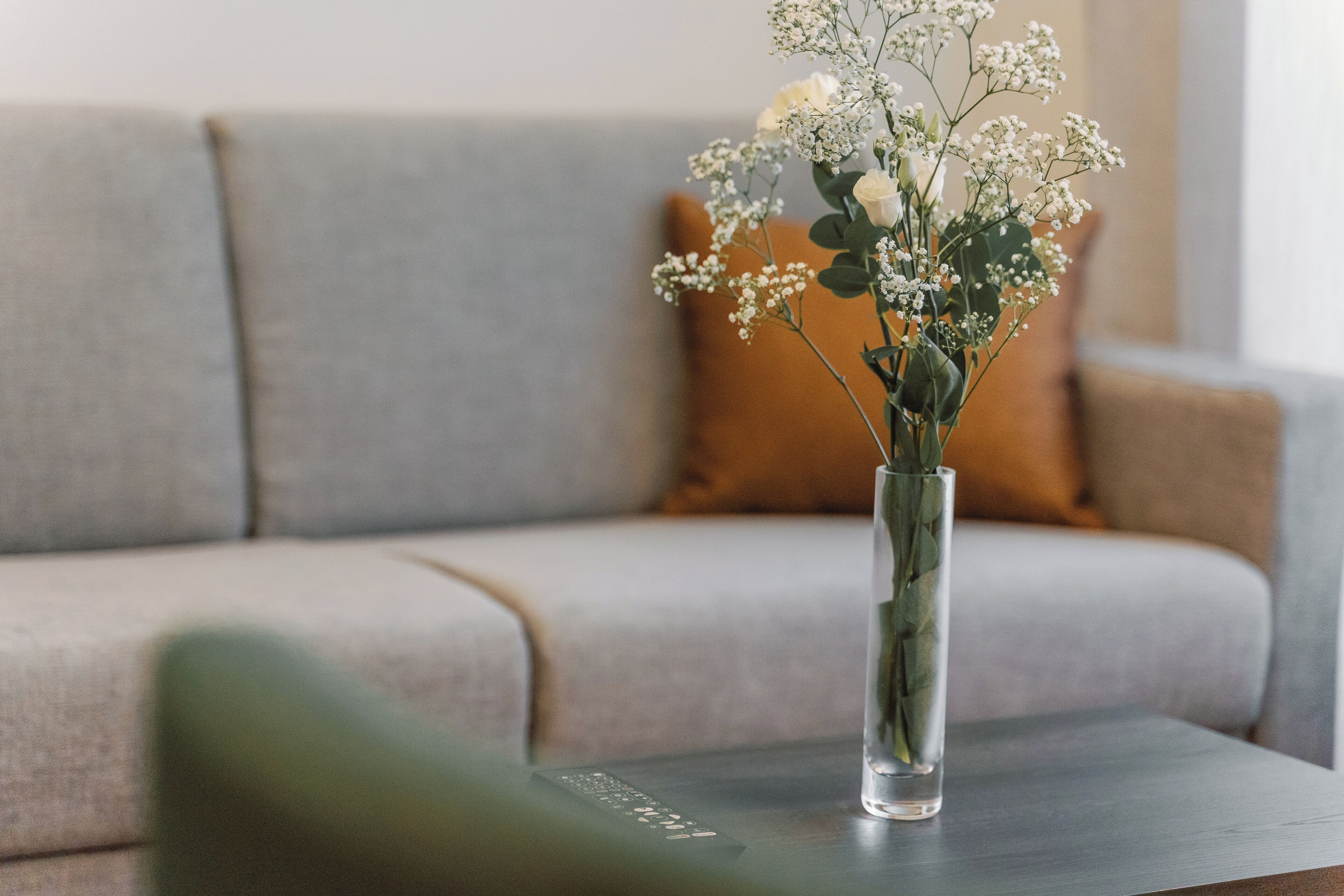 Um vaso de vidro transparente com flores brancas e folhas verdes sobre uma mesa.