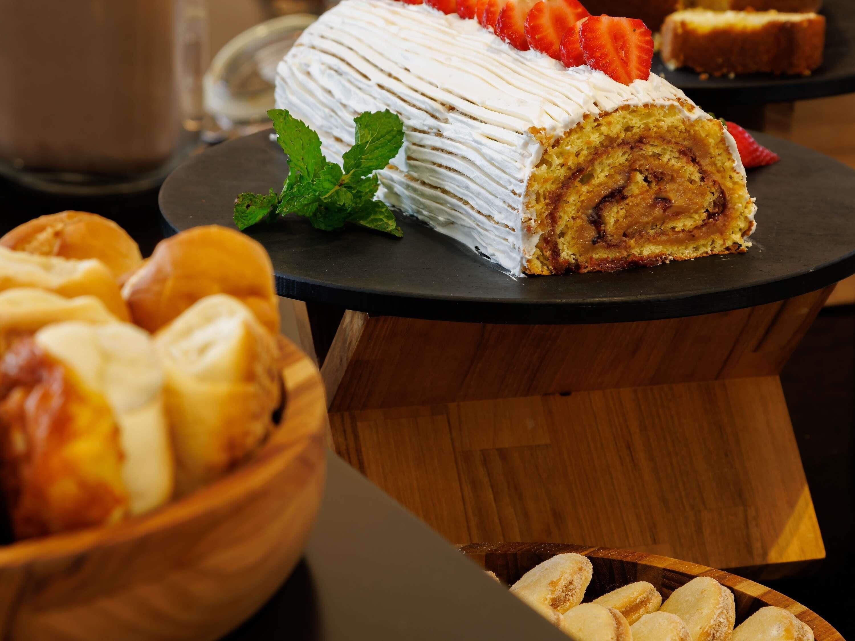 Uma mesa com sobremesas, incluindo um rolo de bolo, morangos e doces.