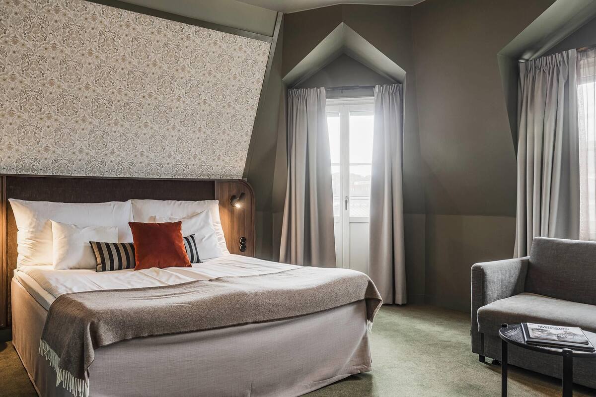 Quarto de hotel moderno com uma cama grande, um espaço de estar e vista para a cidade.