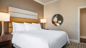 Quarto de hotel com uma cama grande, duas mesas de cabeceira com abajures, um espelho redondo e um tapete estampado.