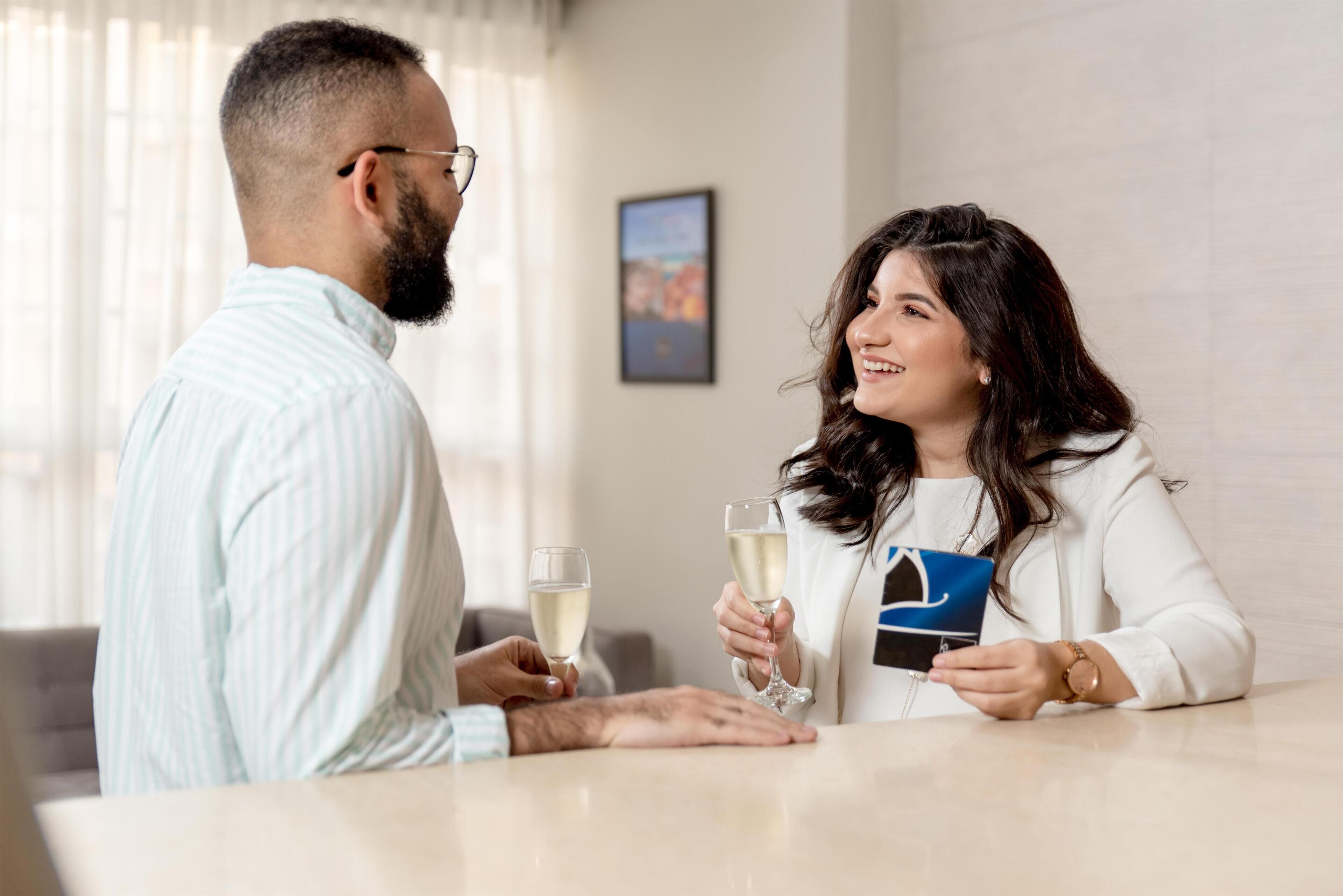 Um homem e uma mulher sentados à mesa com taças de champanhe, segurando um cartão.