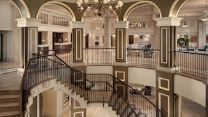 Um interior imponente com teto circular central, escada com corrimão e um candelabro.