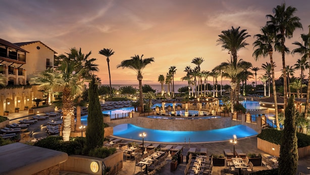 Resort com várias piscinas, palmeiras e áreas de refeições ao ar livre.