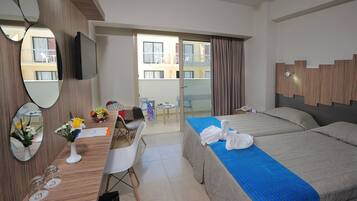 Quarto de hotel com duas camas, uma escrivaninha com cadeira, um espelho e uma varanda com vista para o edifício.