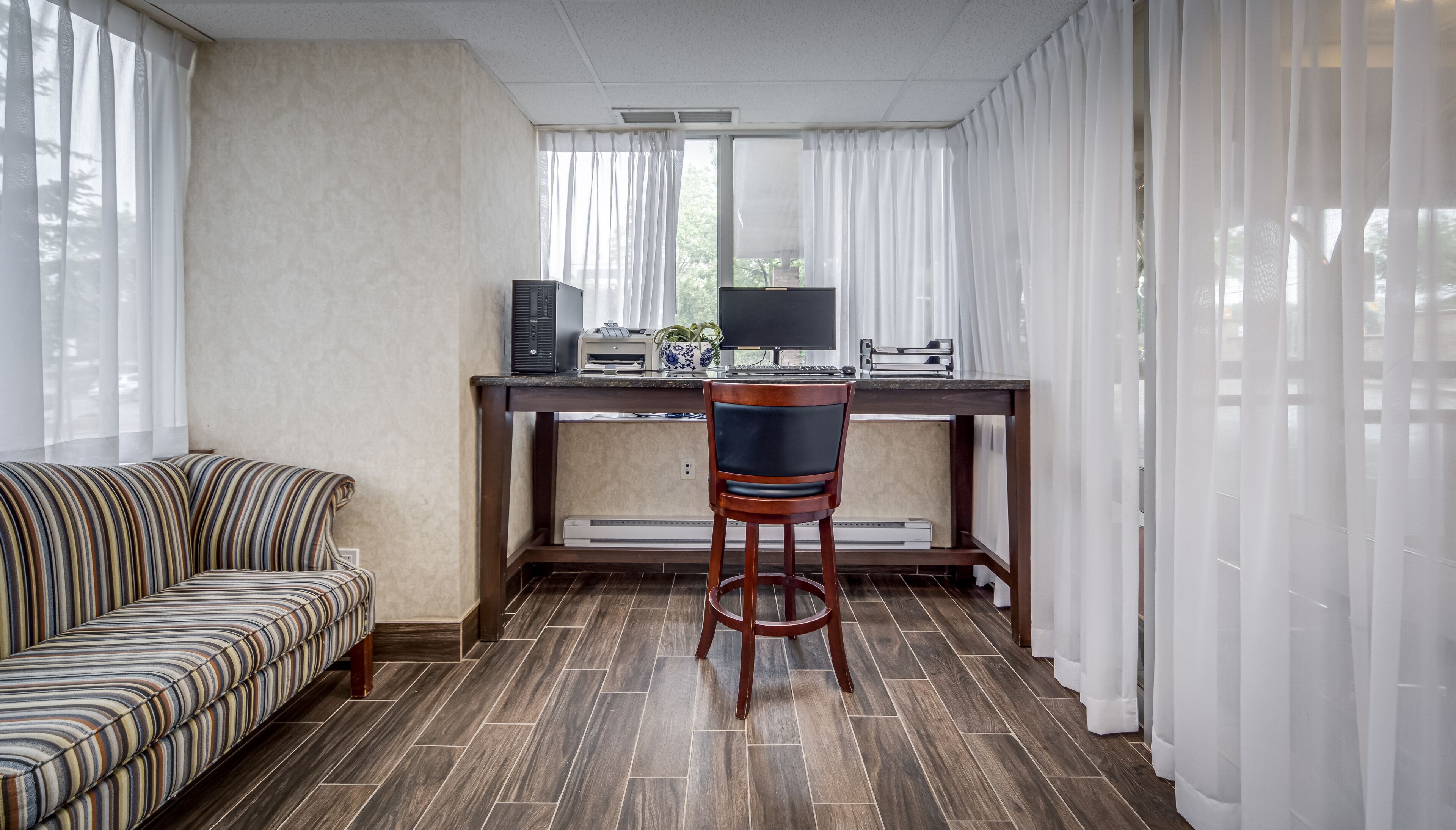 Um espaço de escritório moderno com uma mesa, computador, impressora e um sofá listrado.