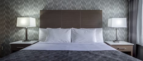 Quarto de hotel com uma cama grande, duas mesas de cabeceira com luminárias, uma cabeceira de madeira e papel de parede com padrão losango.