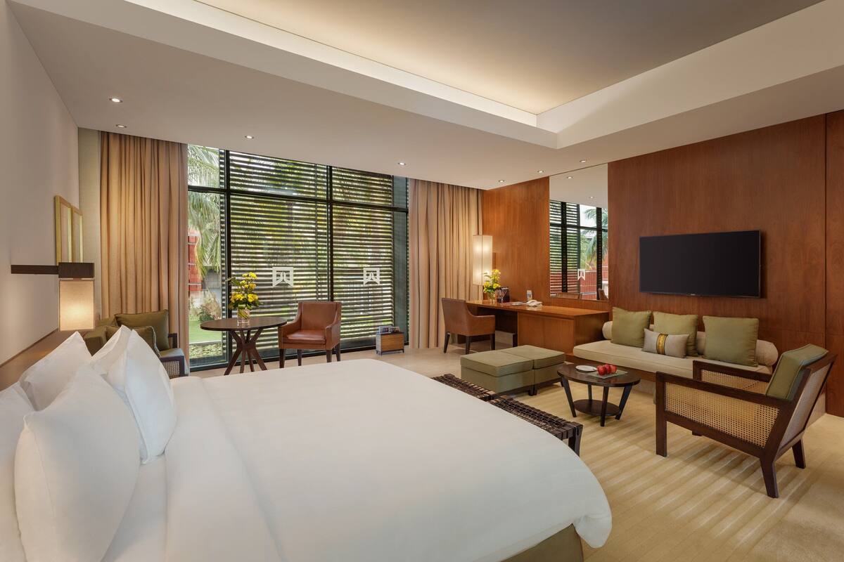 Quarto de hotel moderno com uma cama grande, uma escrivaninha, um sofá e uma televisão.