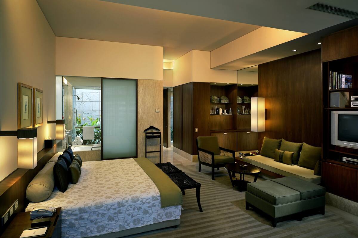 Quarto de hotel moderno com uma cama grande, um sofá, uma TV e uma estante.